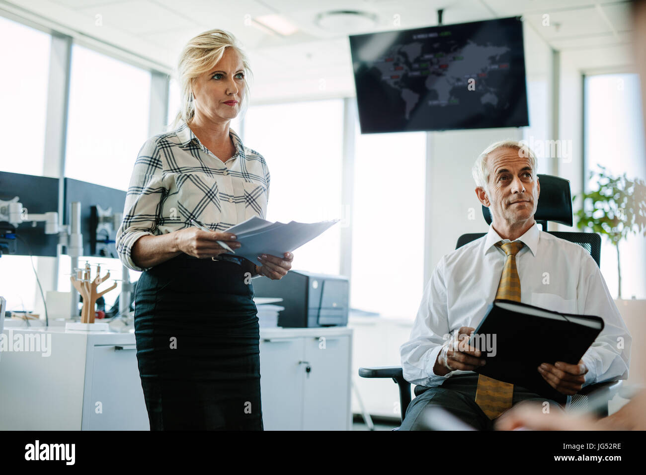Senior businessman sitting in chair with female secretary standing by ...
