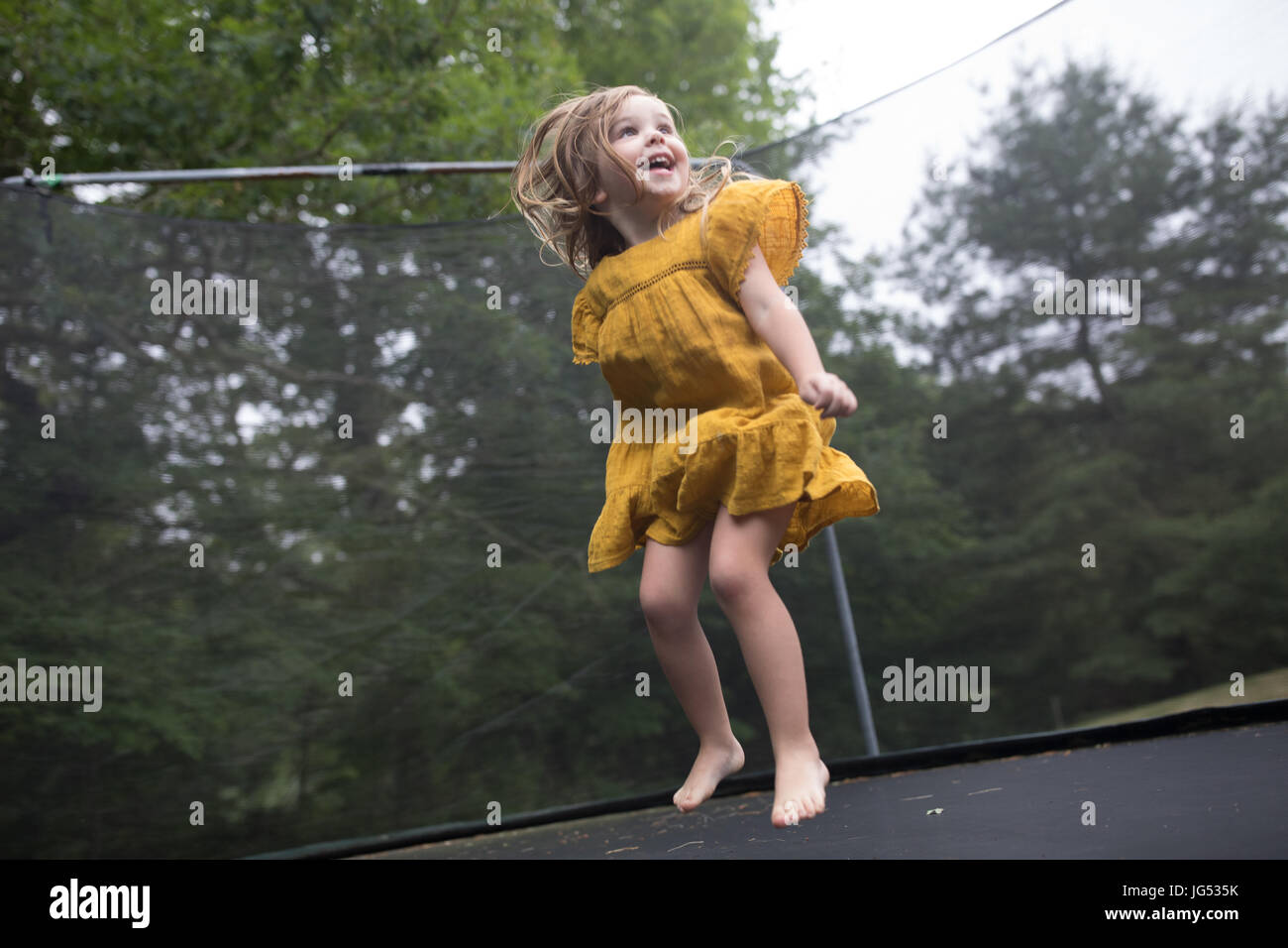 Little girl in yellow dress jumping on the trampoline Stock Photo - Alamy
