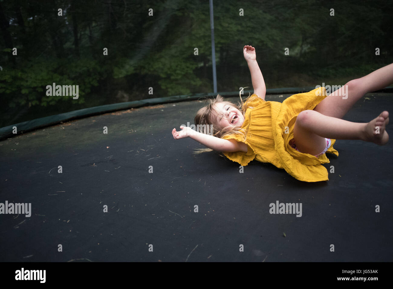 Little girl in yellow dress jumping on the trampoline Stock Photo - Alamy