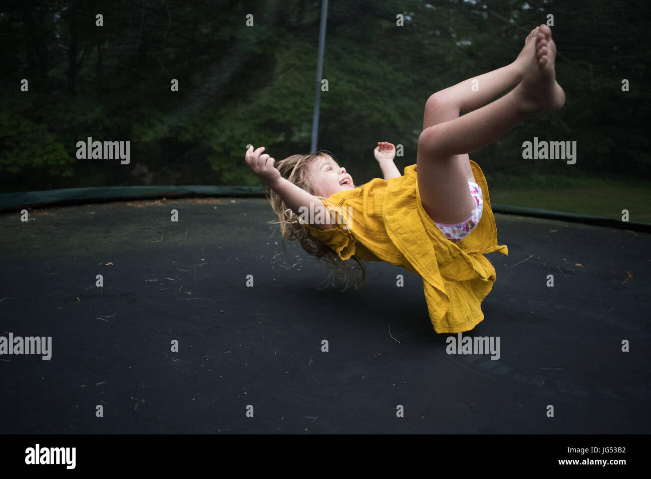 Little girl in yellow dress jumping on the trampoline Stock Photo - Alamy