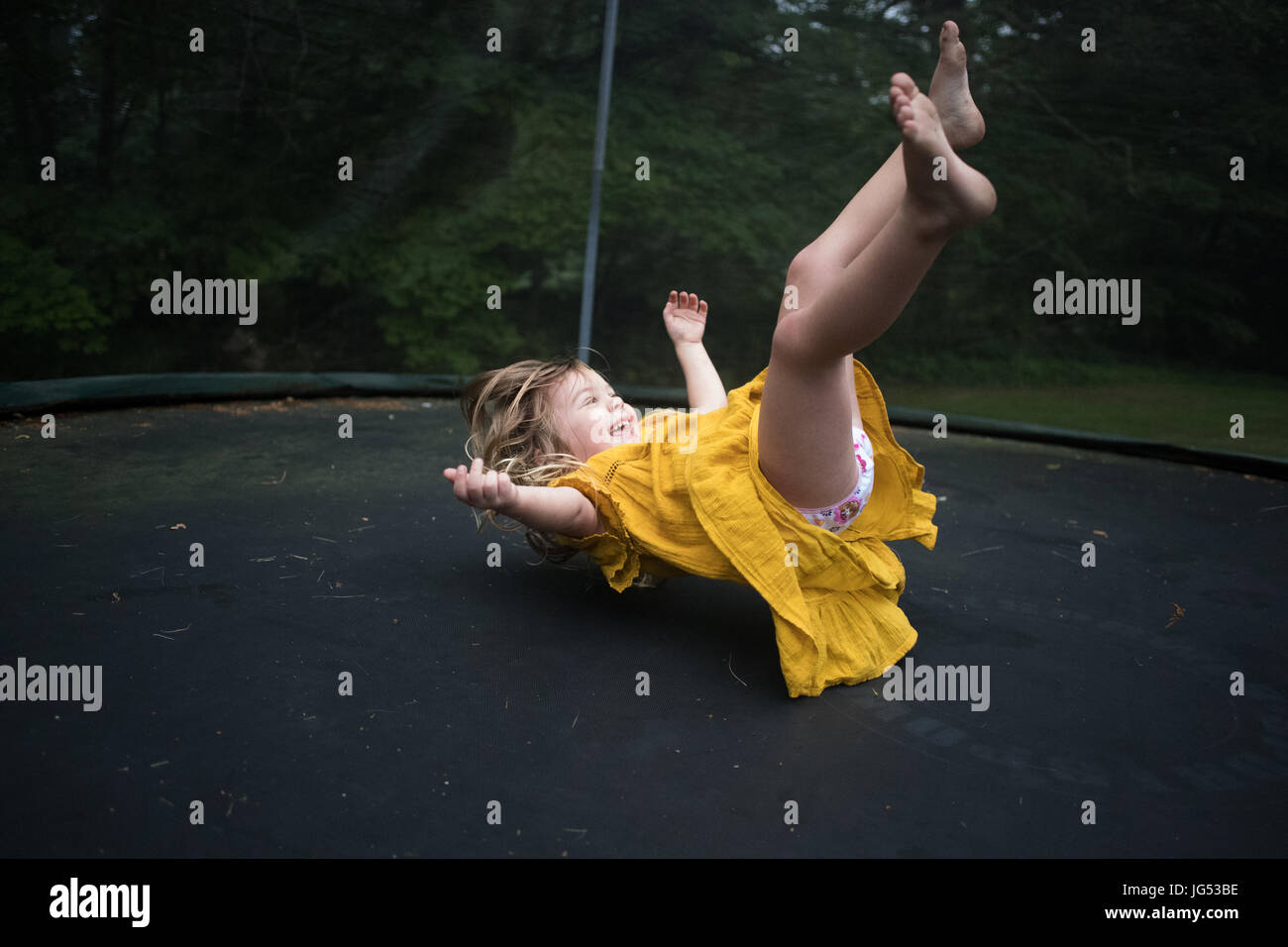 Little girl in yellow dress jumping on the trampoline Stock Photo - Alamy