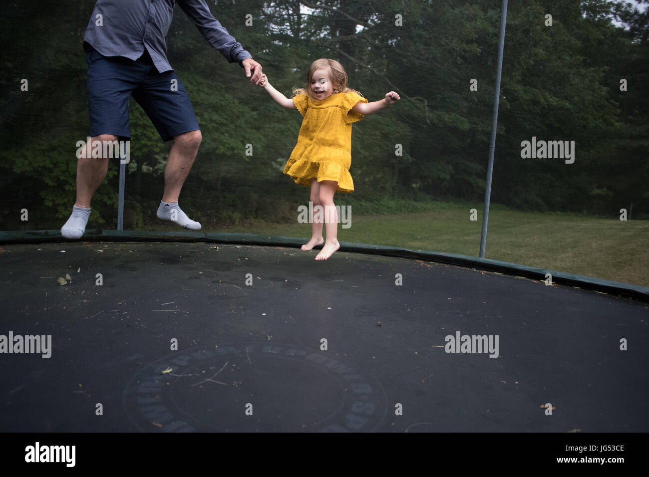Little girl in yellow dress jumping on the trampoline Stock Photo - Alamy