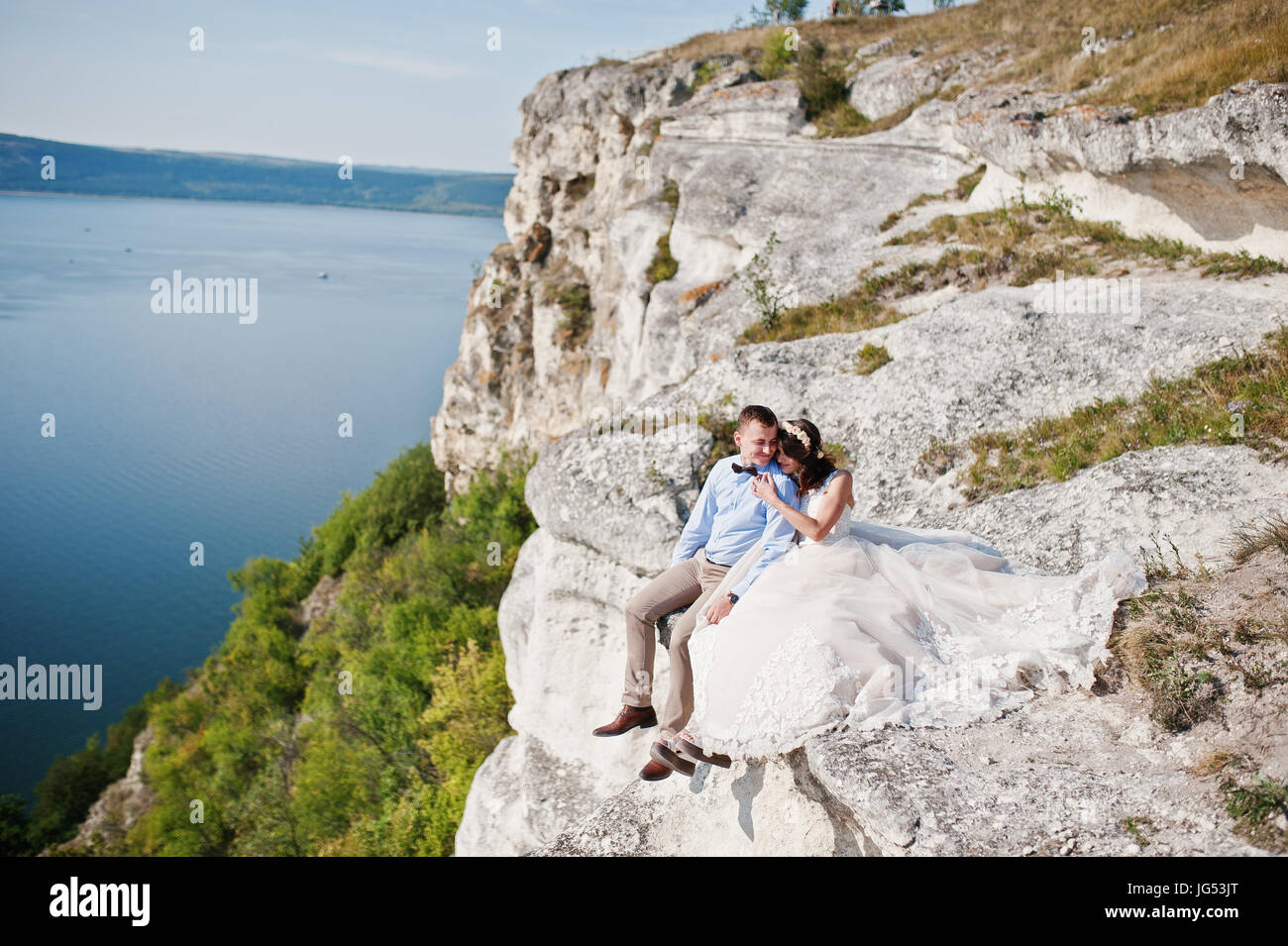 Stunning young wedding couple sitting on the edge of the cliff with a ...