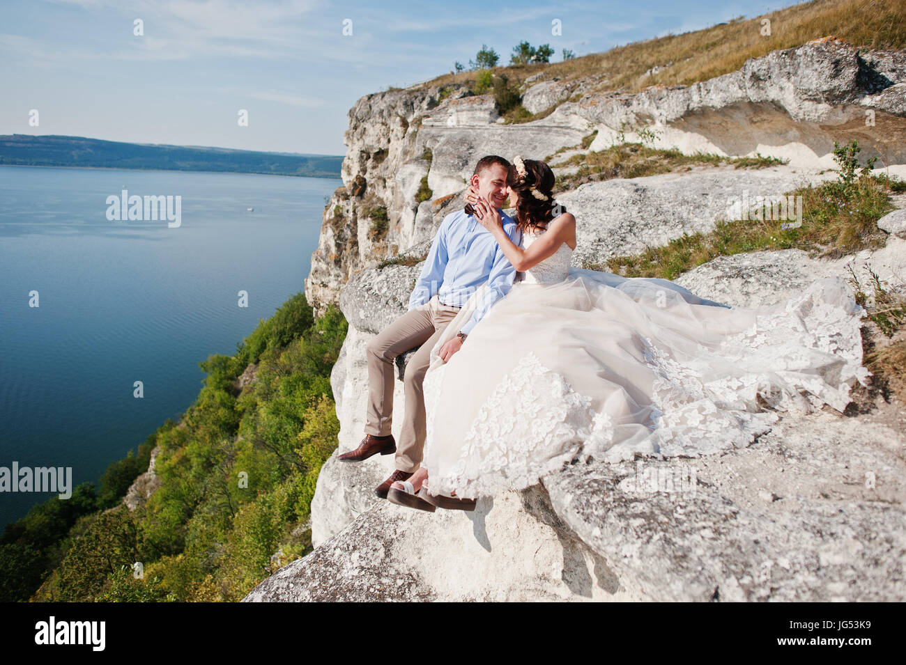 Stunning young wedding couple sitting on the edge of the cliff with a ...