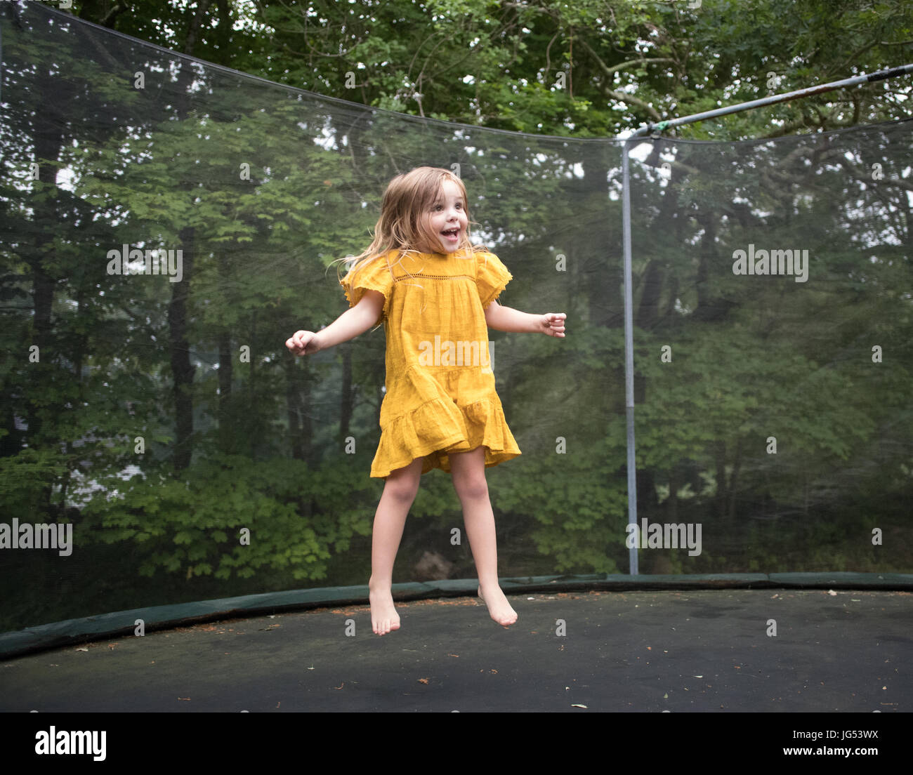 Little girl in yellow dress jumping on the trampoline Stock Photo - Alamy