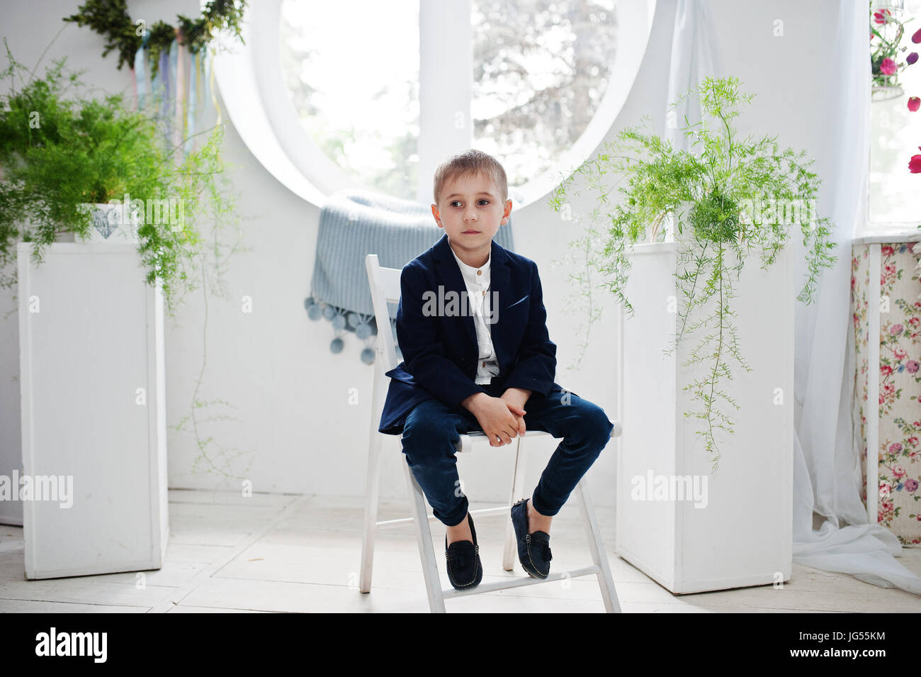 Portrait of an adorable little boy sitting on the chair in white room ...