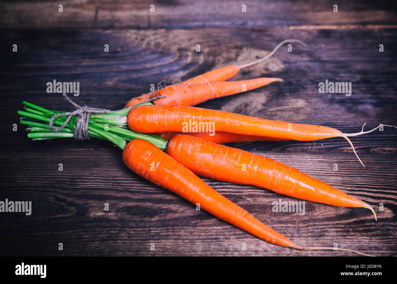 Fresh carrots tied with a rope in a bunch on a brown wooden background ...
