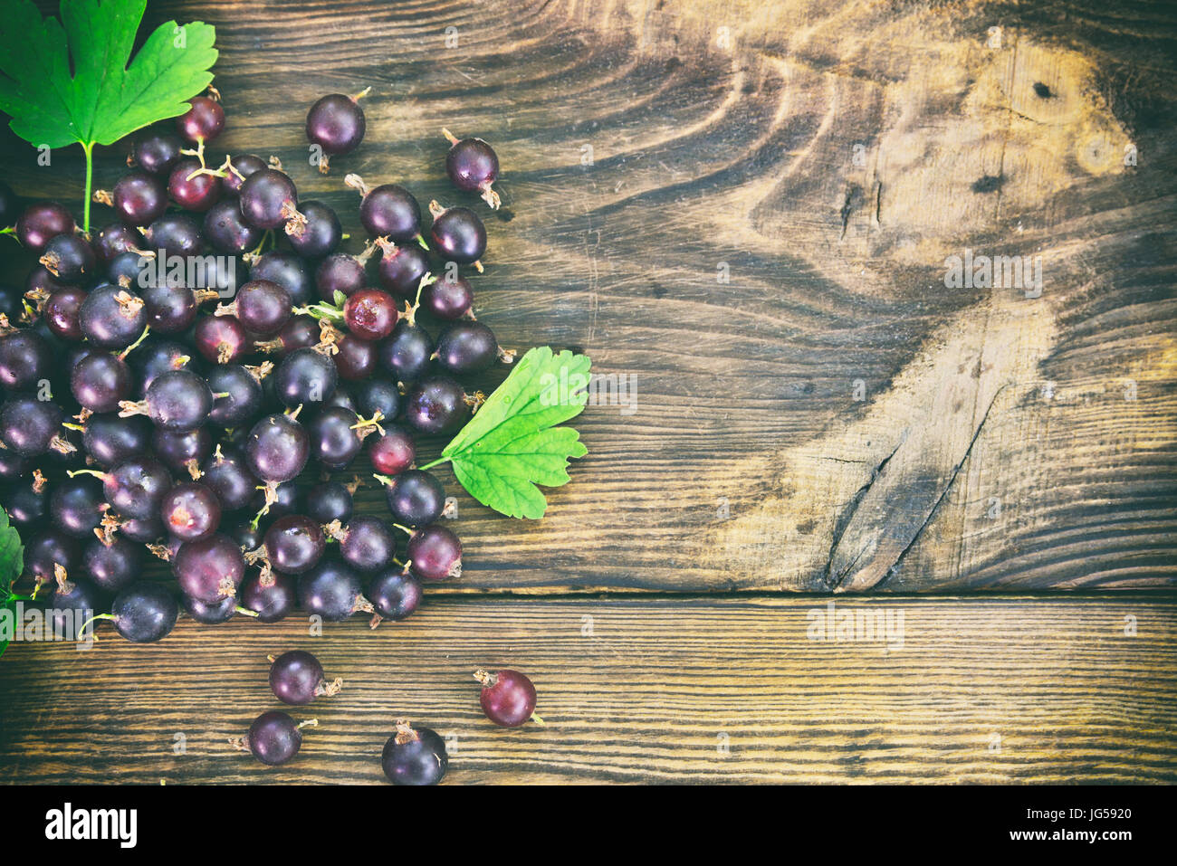 Black currant with green leaves on a brown wooden background, empty ...