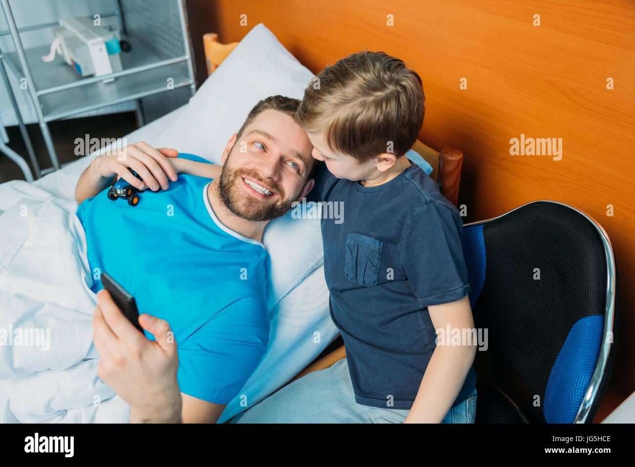 father with son embracing while laying on hospital bed at ward ...