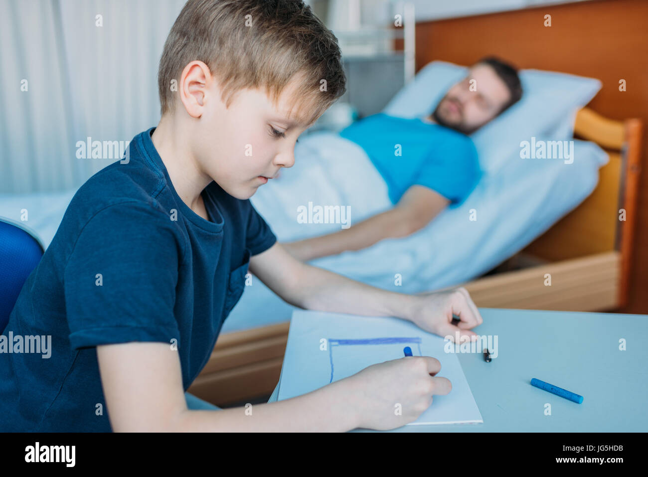 son drawing pictures while sick father laying on hospital bed at ward ...
