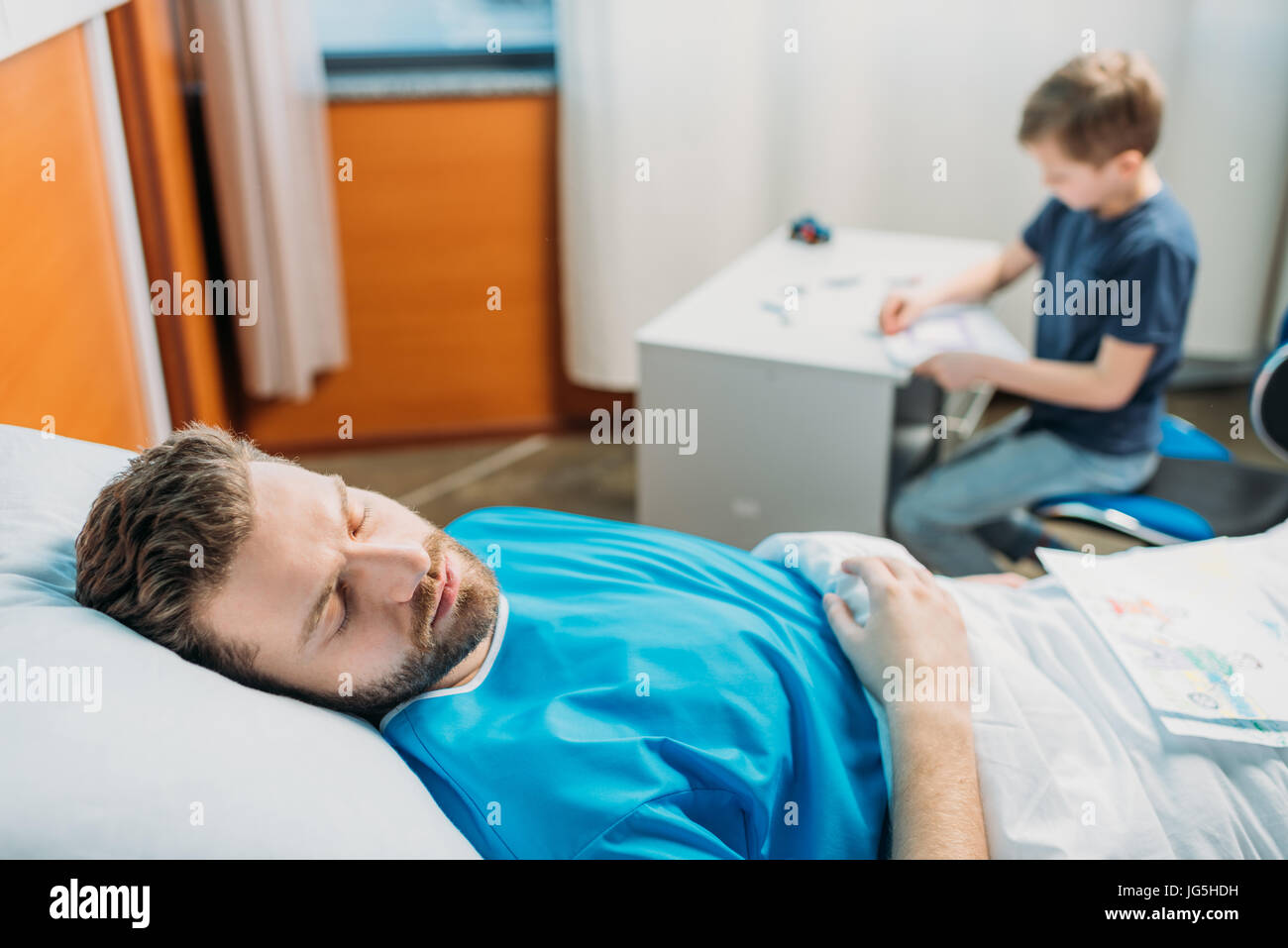son drawing pictures while sick father laying on hospital bed at ward ...