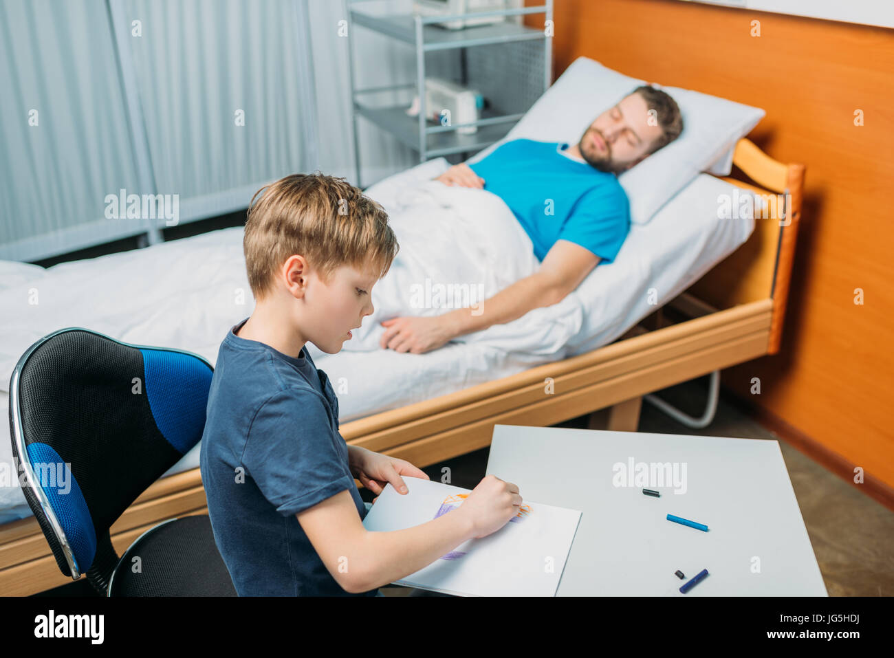 son drawing pictures while sick father laying on hospital bed at ward ...