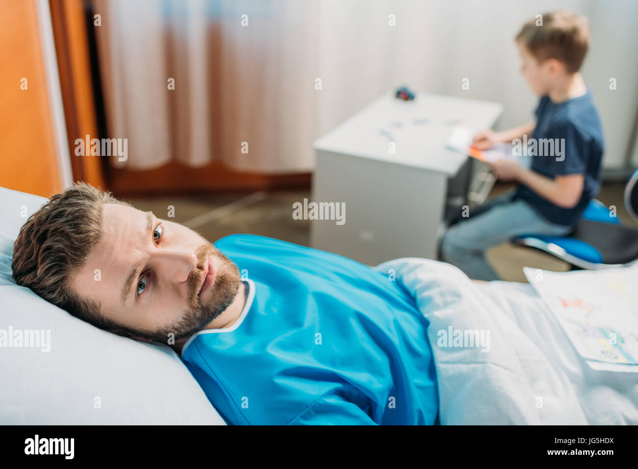 son drawing pictures while sick father laying on hospital bed at ward ...