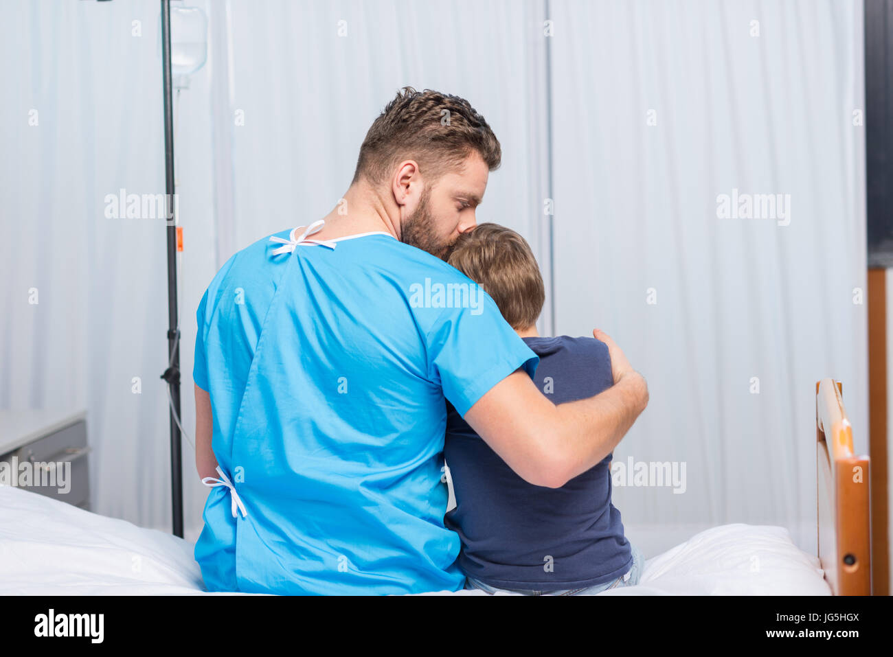 Back view of sick father and little son sitting together on hospital ...