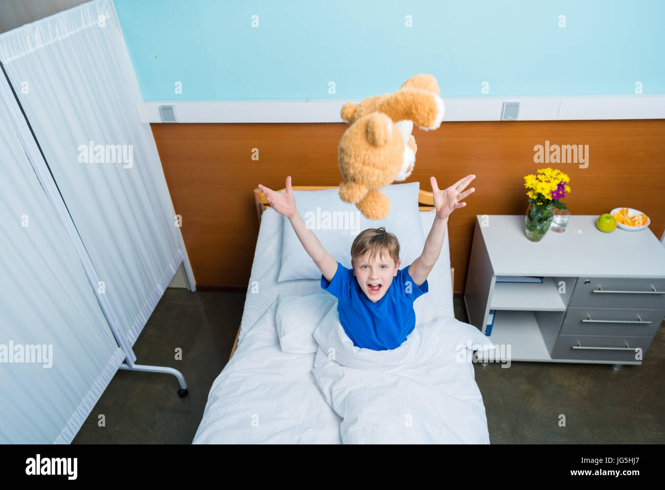 High angle view of cheerful little boy raising hands and throwing teddy ...