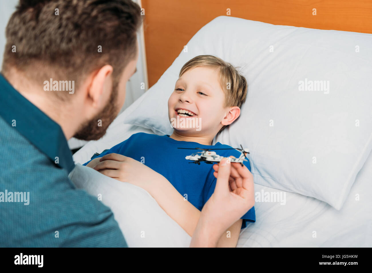 Smiling father playing with sick little boy lying in hospital bed, dad ...