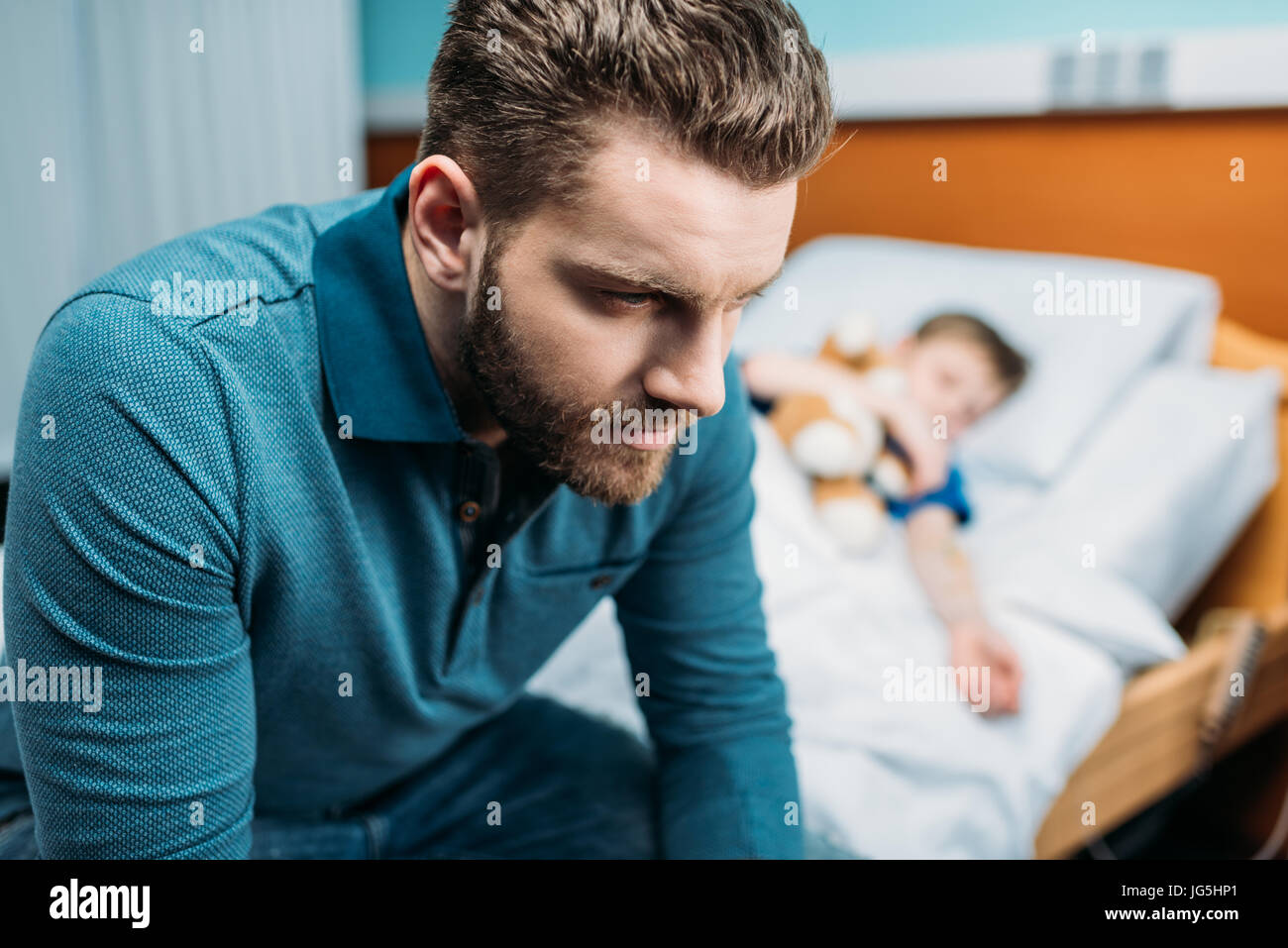 side view of thoughtful dad sitting near sick son in hospital bed Stock ...