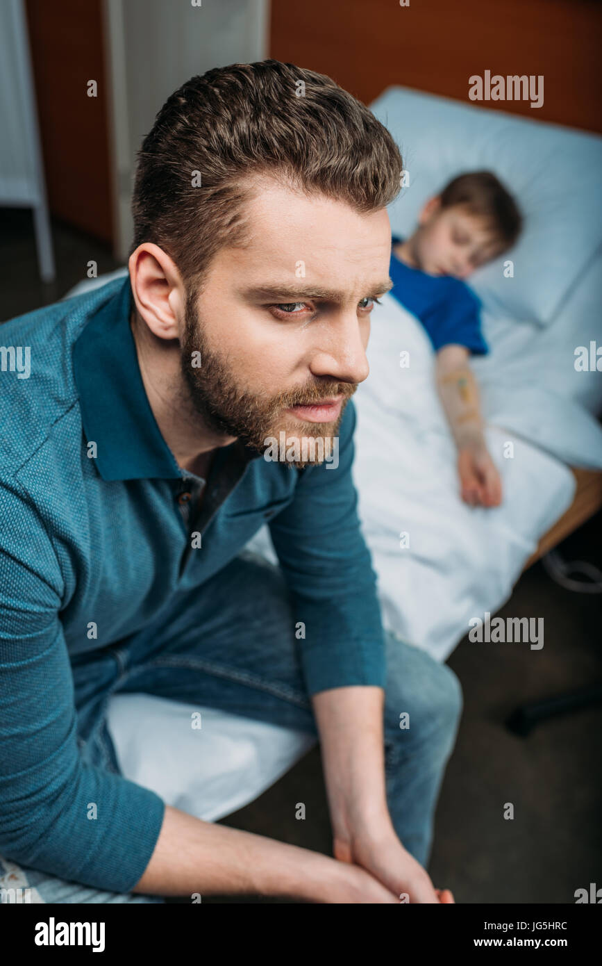 portrait of thoughtful dad sitting near sick son in hospital bed Stock ...