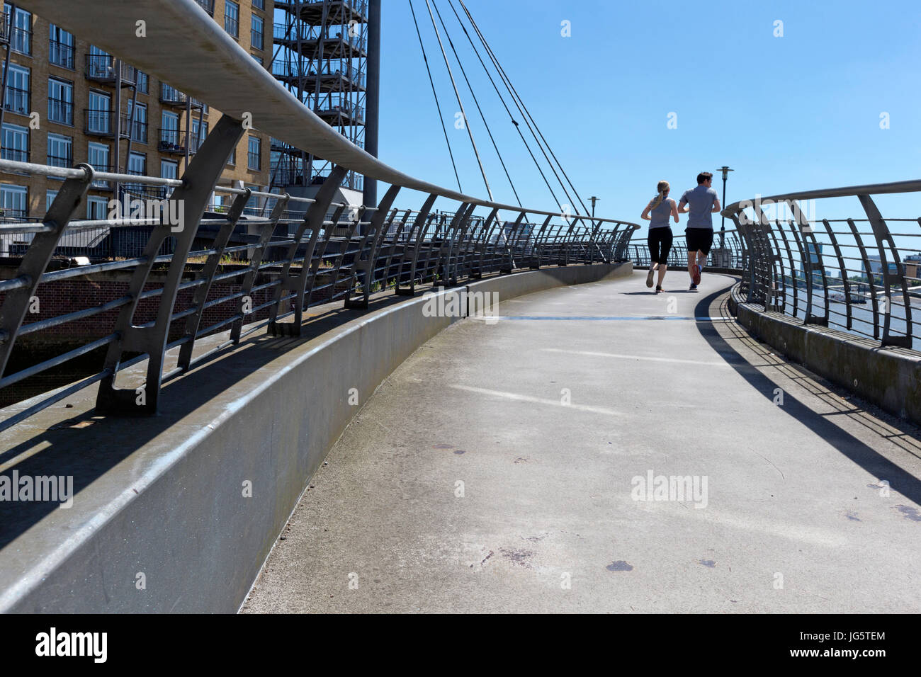 Two people running over a pedestrian bridge over an inlet of the river ...
