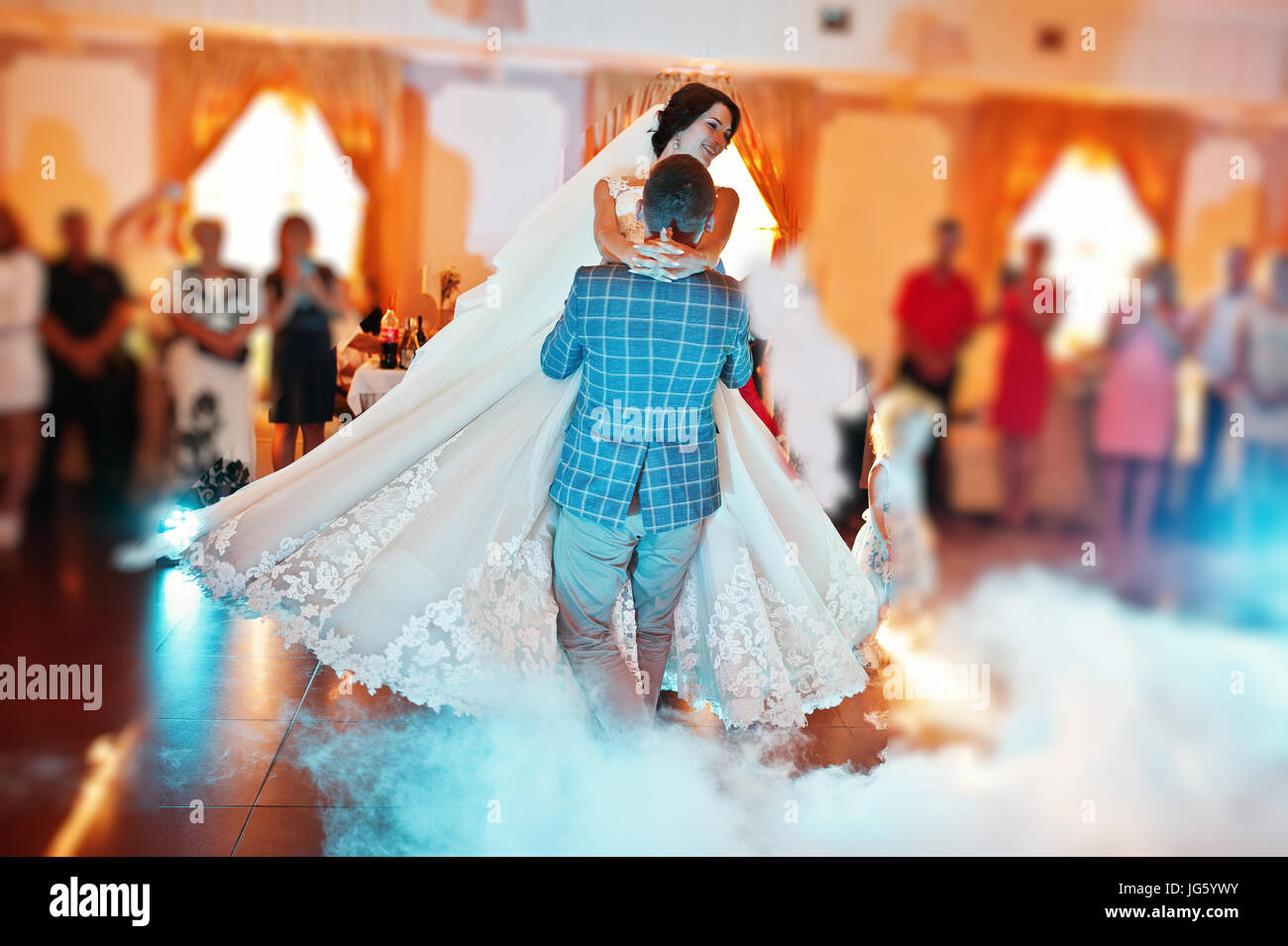 Beautiful wedding couple dancing their first dance in a restaurant with people in the background ...