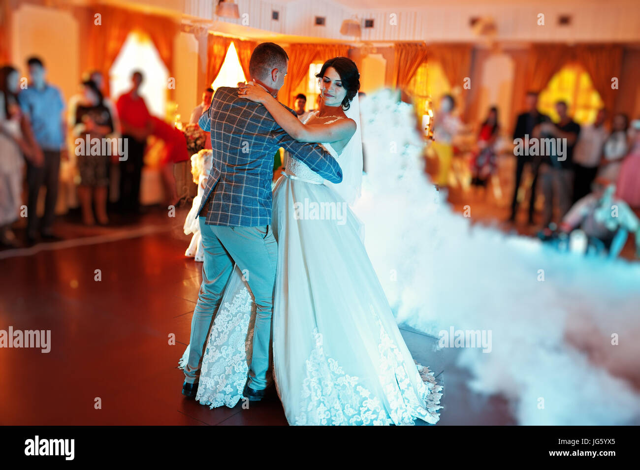 Beautiful wedding couple dancing their first dance in a restaurant with people in the background ...