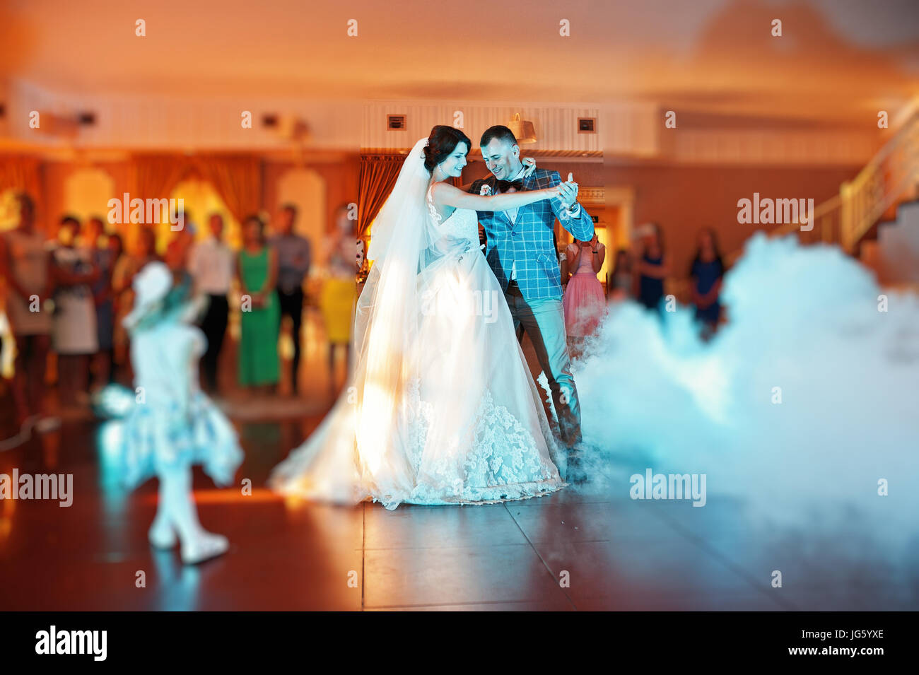 Beautiful wedding couple dancing their first dance in a restaurant with people in the background ...