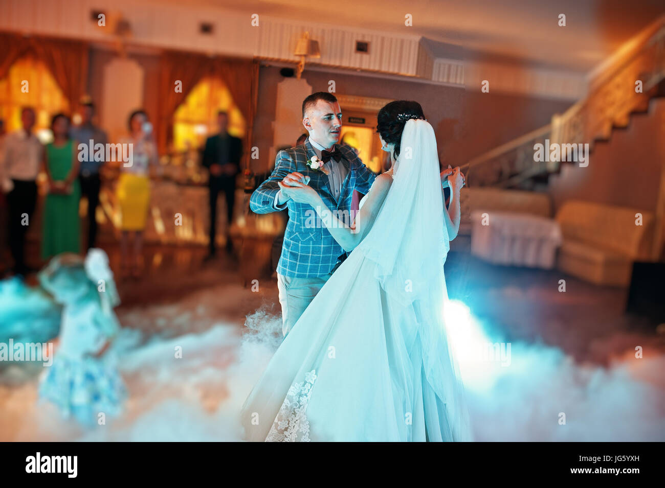 Beautiful wedding couple dancing their first dance in a restaurant with people in the background ...