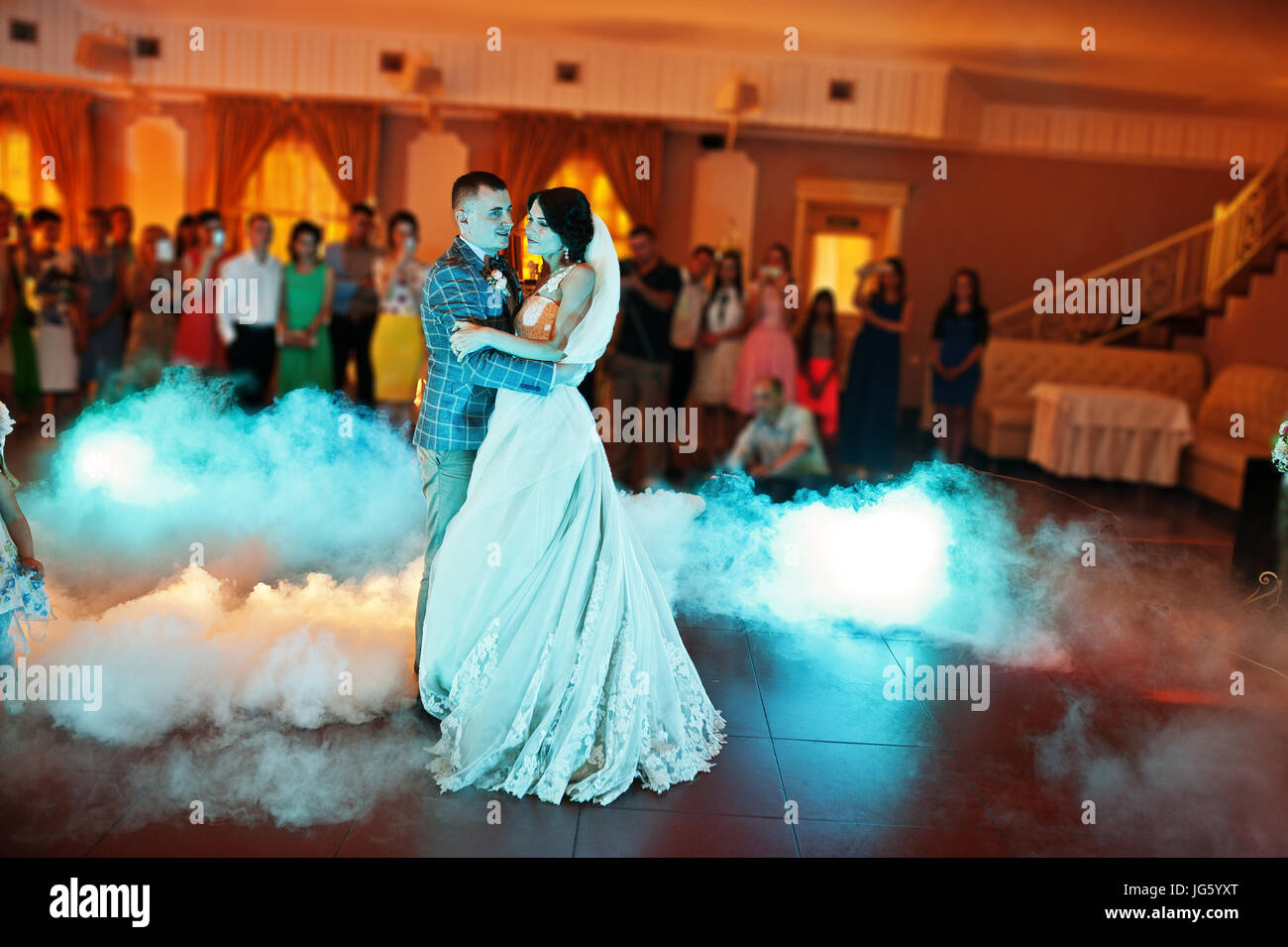Beautiful wedding couple dancing their first dance in a restaurant with people in the background ...