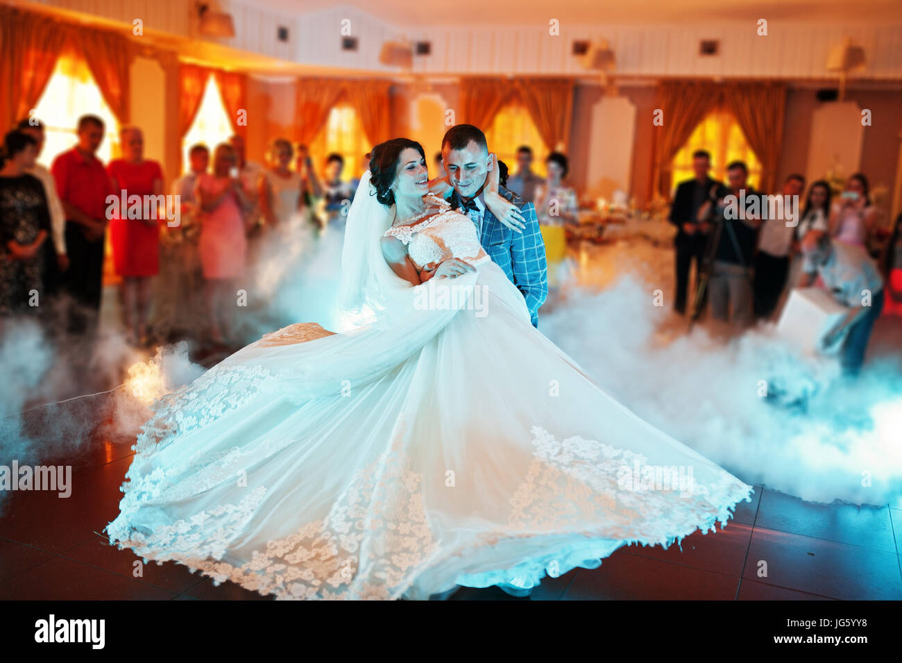 Beautiful wedding couple dancing their first dance in a restaurant with people in the background ...
