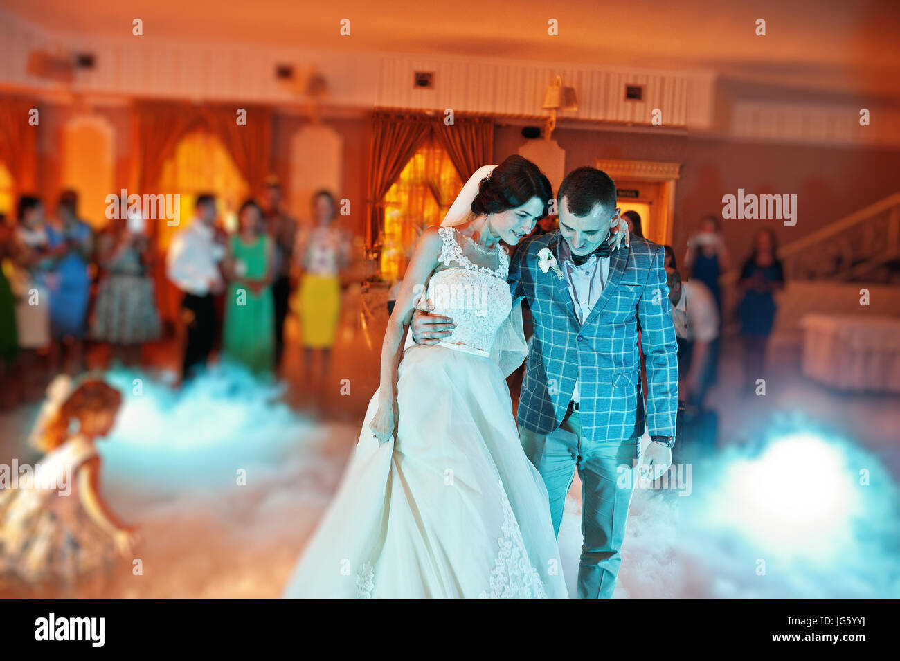 Beautiful wedding couple dancing their first dance in a restaurant with people in the background ...