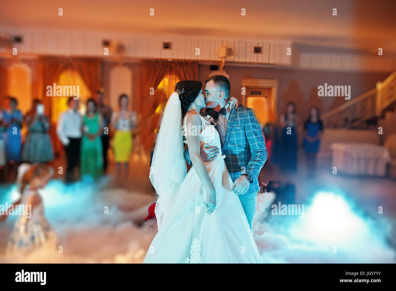 Beautiful wedding couple dancing their first dance in a restaurant with people in the background ...