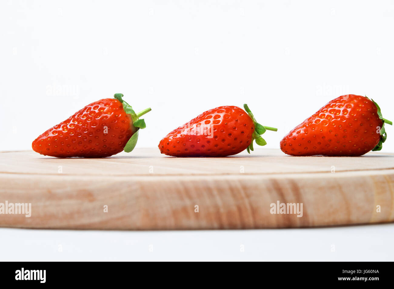 A line of three red strawberries with leaves and short stalks intact ...