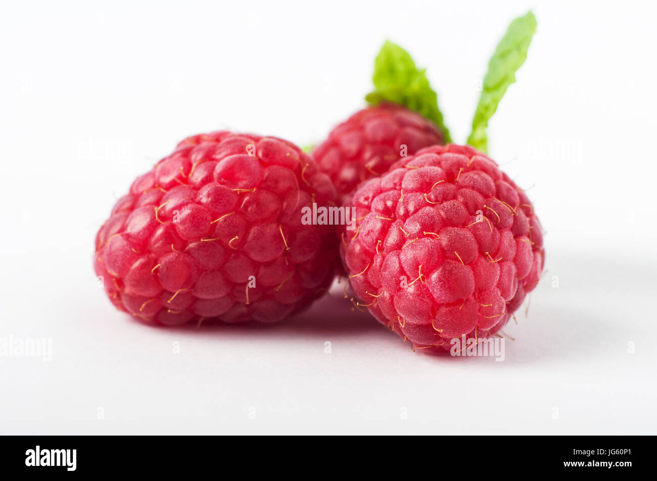 Close up of three raspberry fruits, grouped together with a fresh green ...