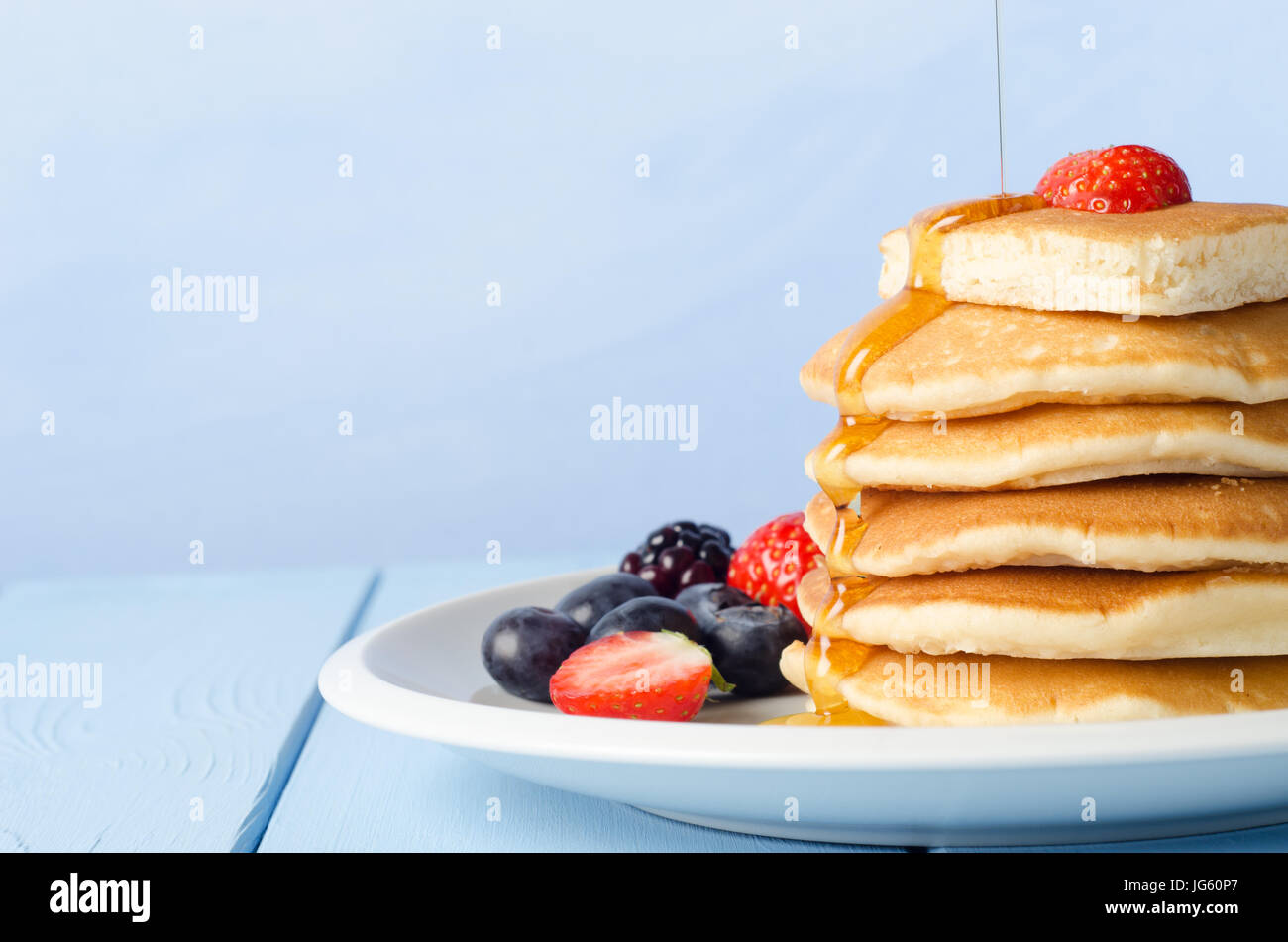 A stack of breakfast pancakes topped with a strawberry, standing on a ...