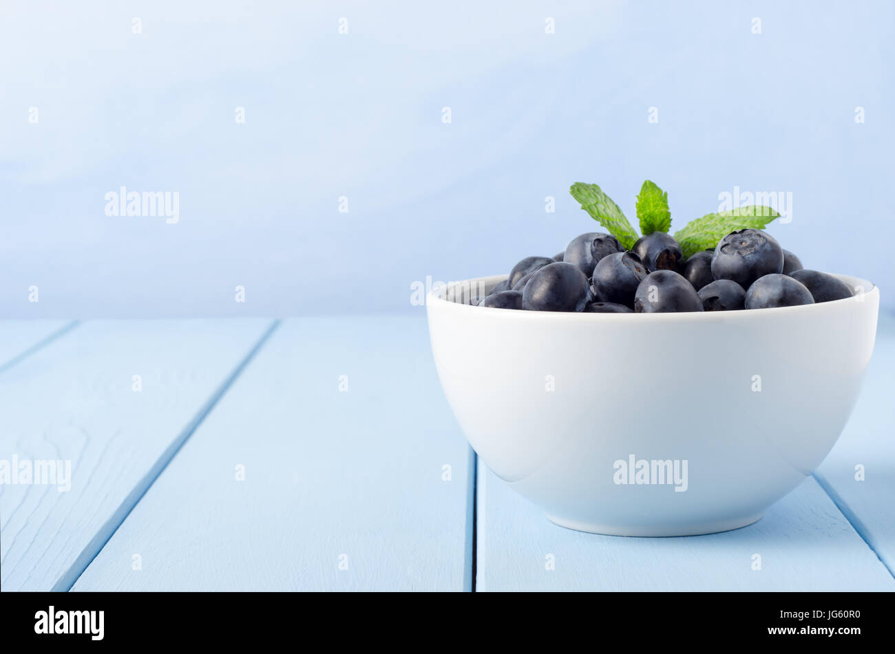 Eye level view of a white bowl of blueberries topped with a sprig of ...