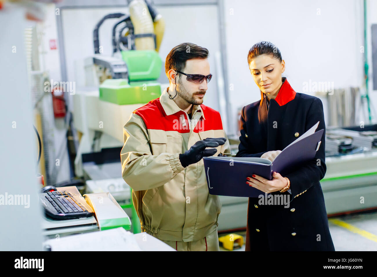 Pretty young woman controlling process in the factory with male worker ...