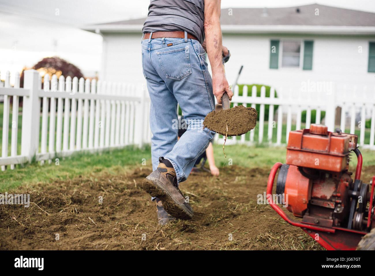 A man shovels dirt in a garden next to a rotatiller Stock Photo - Alamy