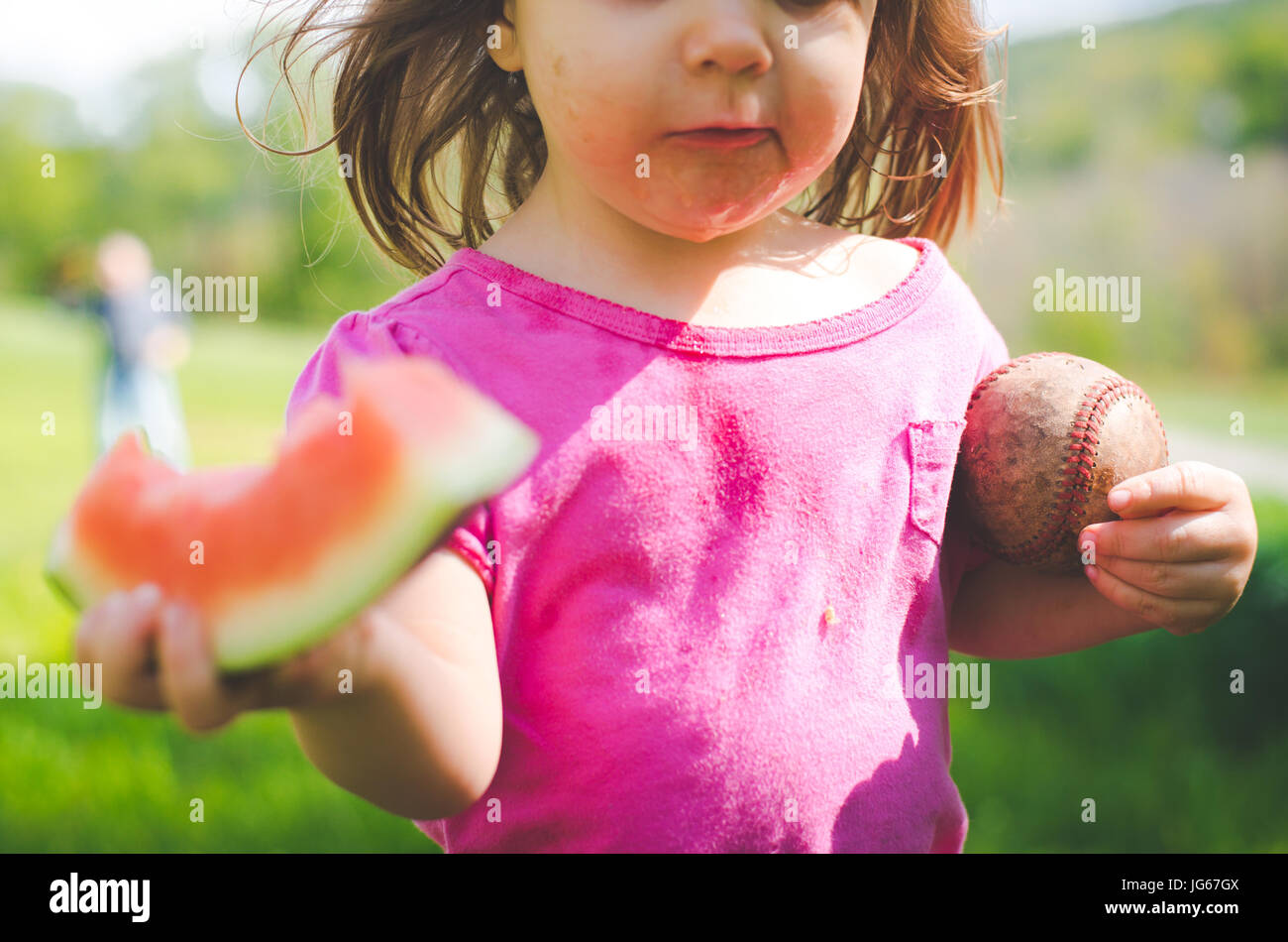 A young girl eats a watermelon and holds a baseball in summer Stock ...