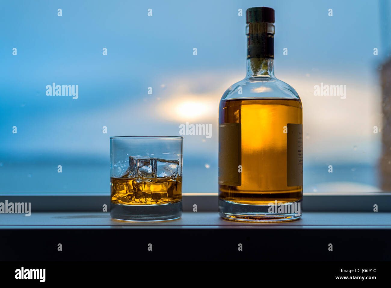 Alcohol drink with ice next to bottle resting on seaside rainy window ...