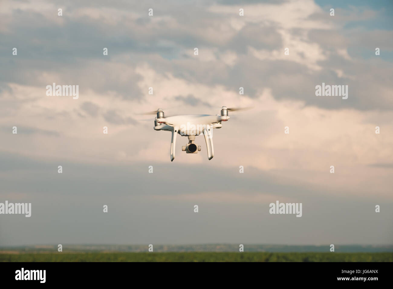 White drone hovering in a bright blue sky. Drone copter flying with ...