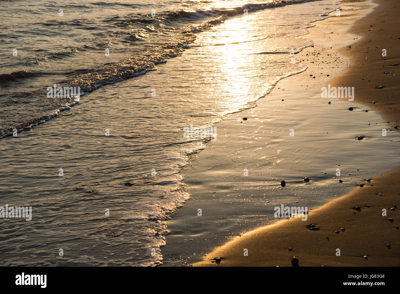 Waves approaching beach sand during golden sunset Stock Photo - Alamy