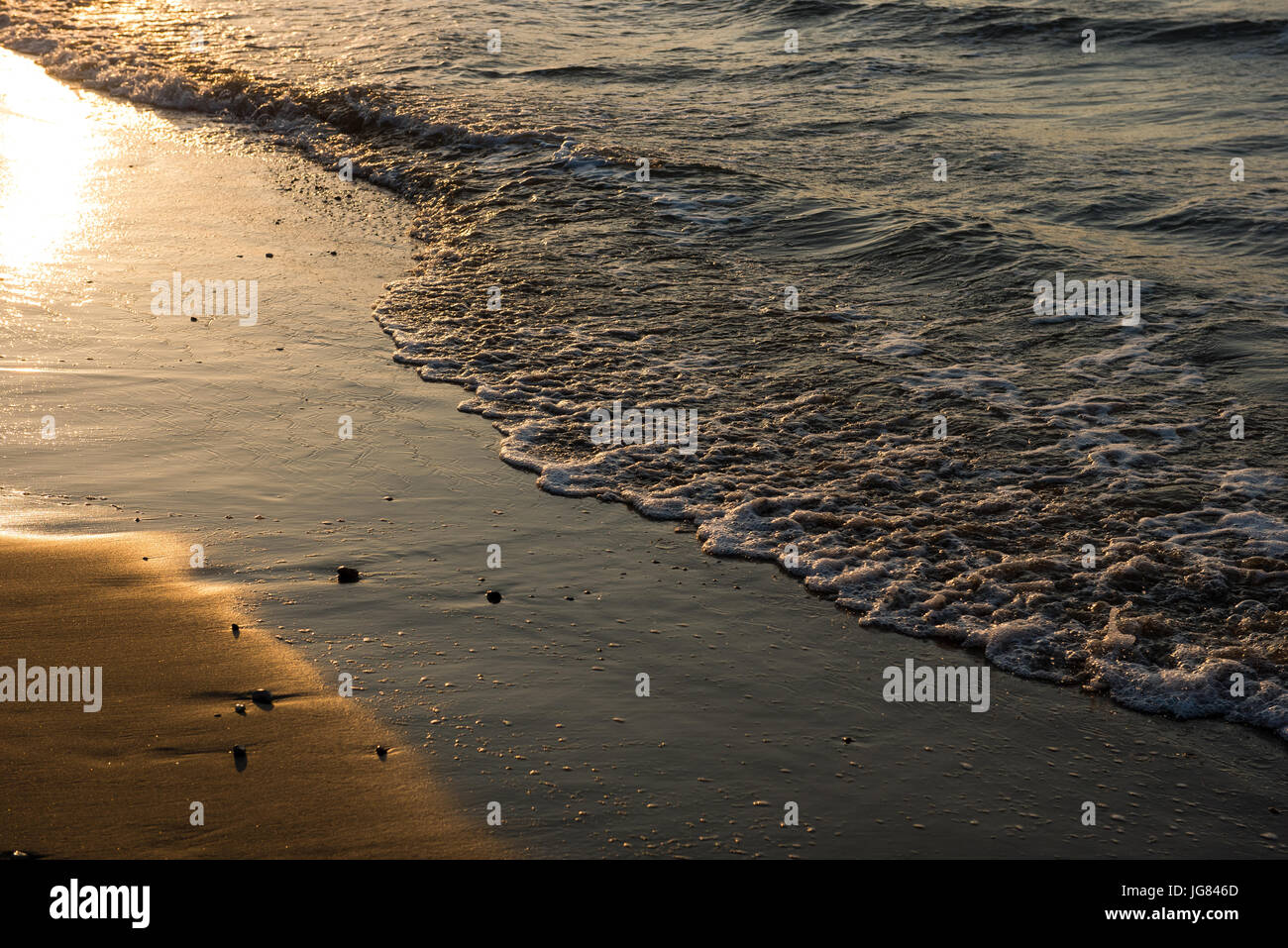 Waves approaching beach sand during golden sunset Stock Photo - Alamy