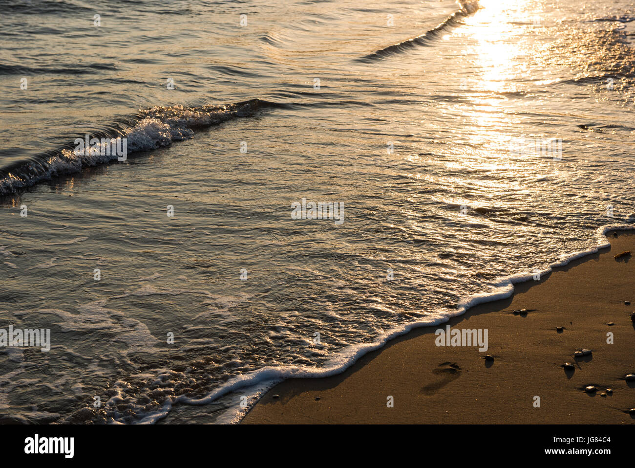 Waves approaching beach sand during golden sunset Stock Photo - Alamy