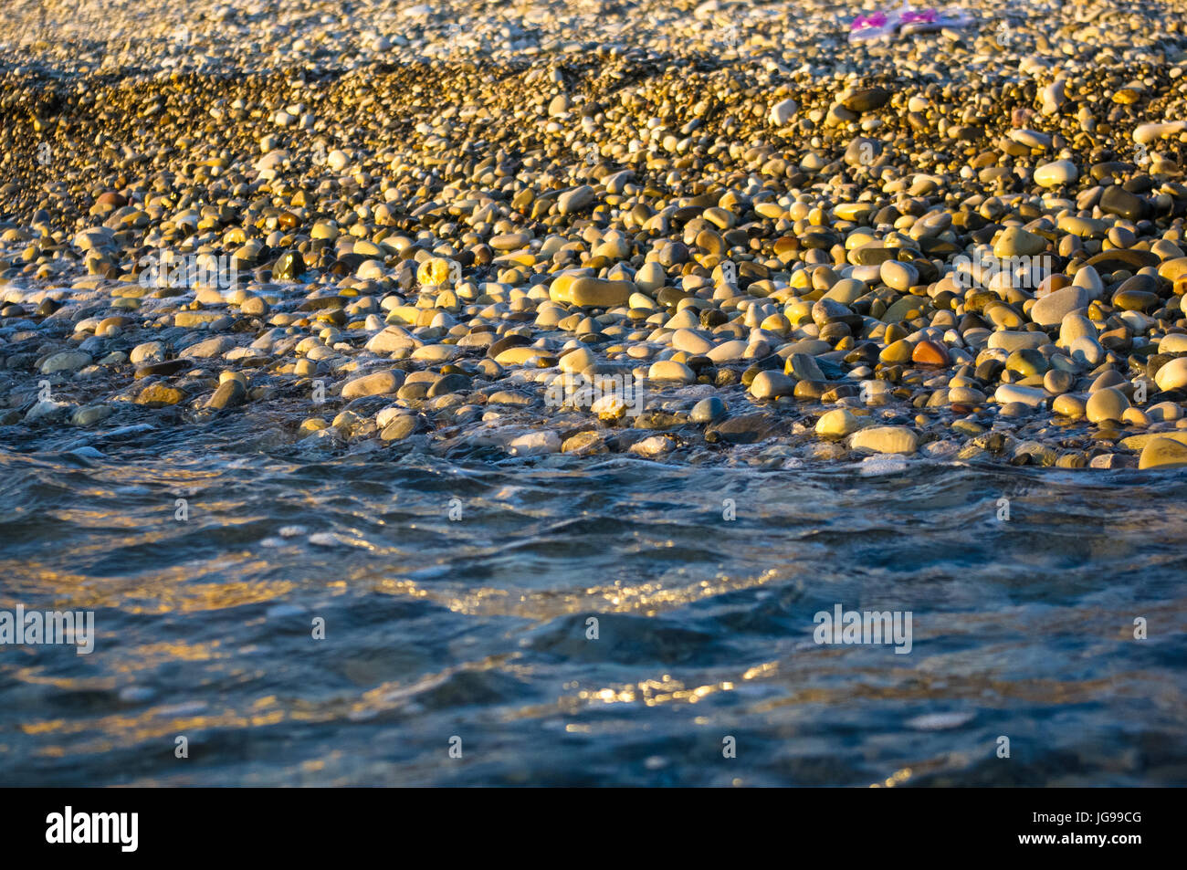 sea pebble beach with multicoloured stones, transparent waves with foam ...