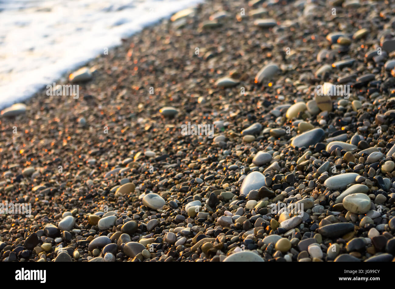 sea pebble beach with multicoloured stones, transparent waves with foam ...