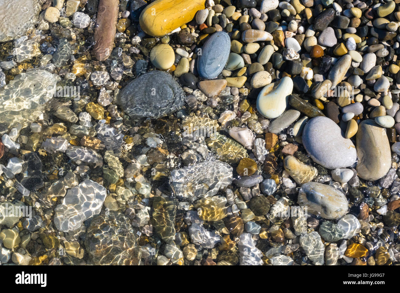 sea pebble beach with multicoloured stones, transparent waves with foam ...