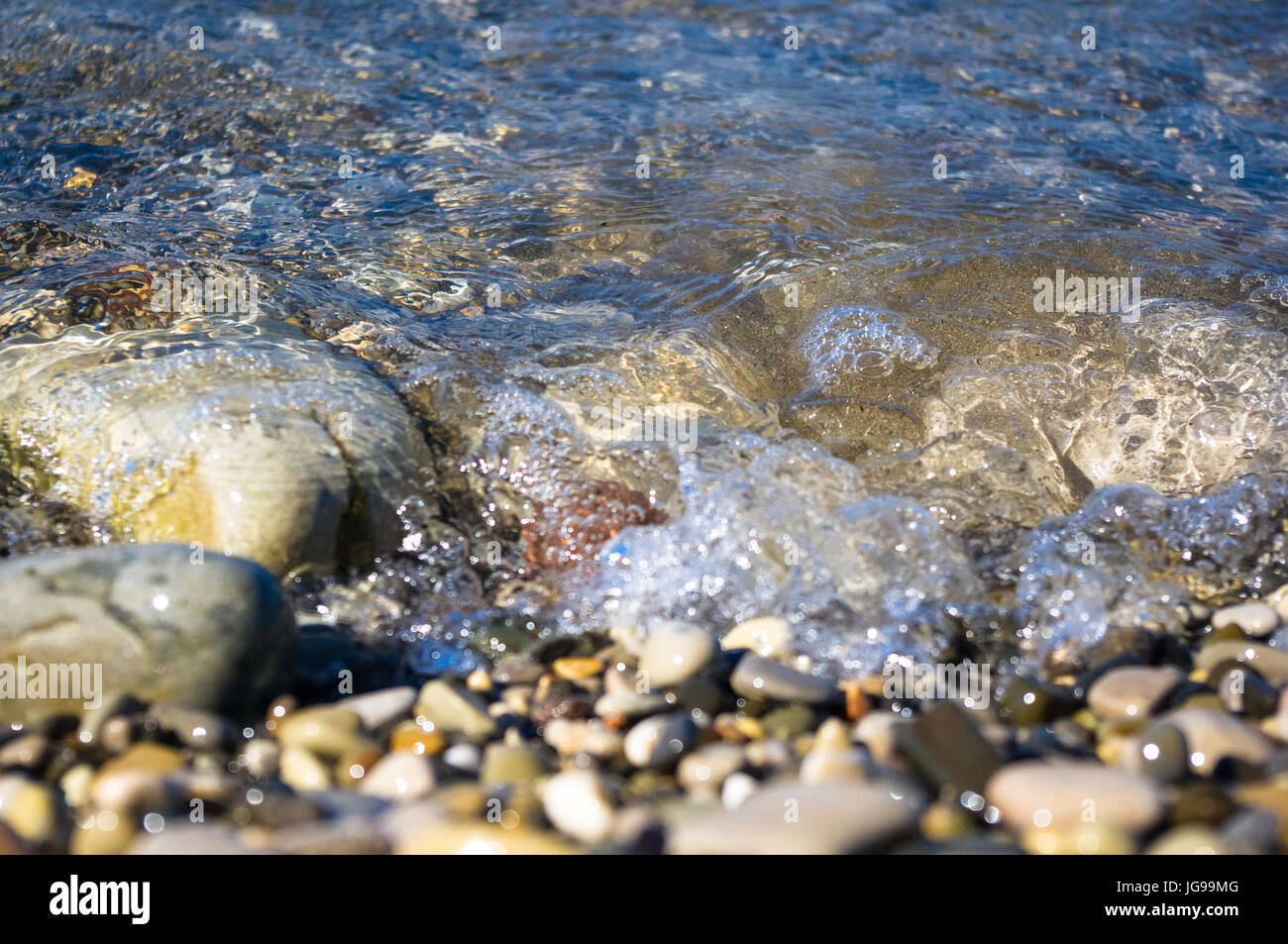 sea pebble beach with multicoloured stones, transparent waves with foam ...