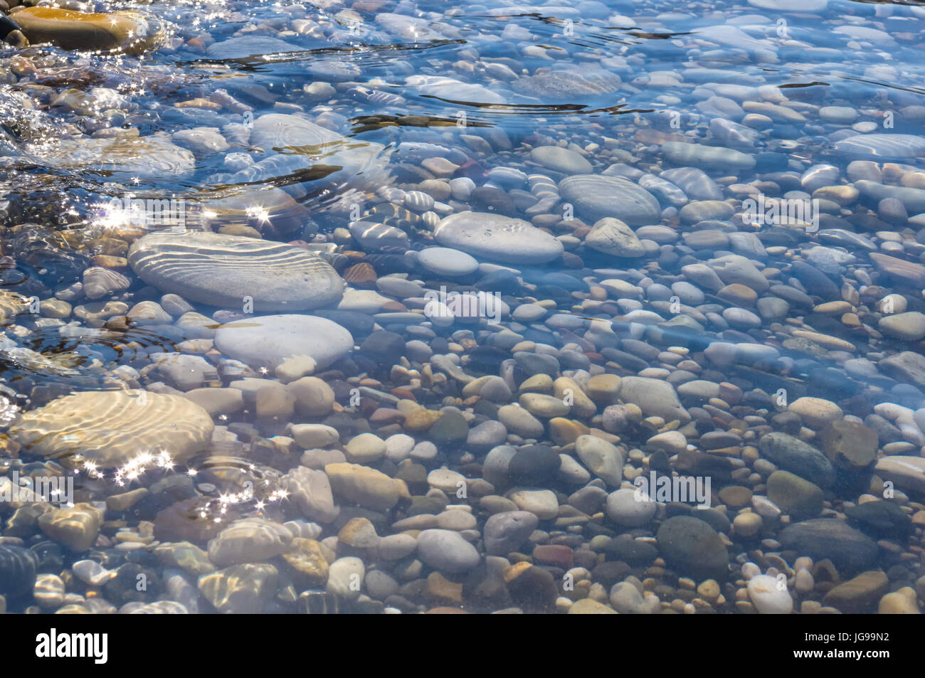 sea pebble beach with multicoloured stones, transparent waves with foam ...
