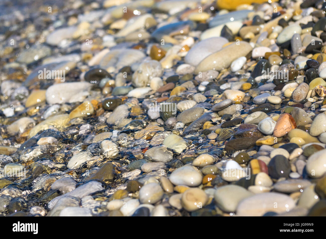 sea pebble beach with multicoloured stones, transparent waves with foam ...