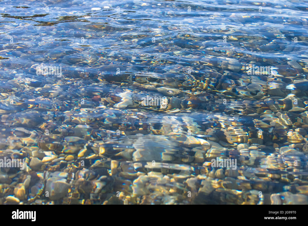 sea pebble beach with multicoloured stones, transparent waves with foam ...